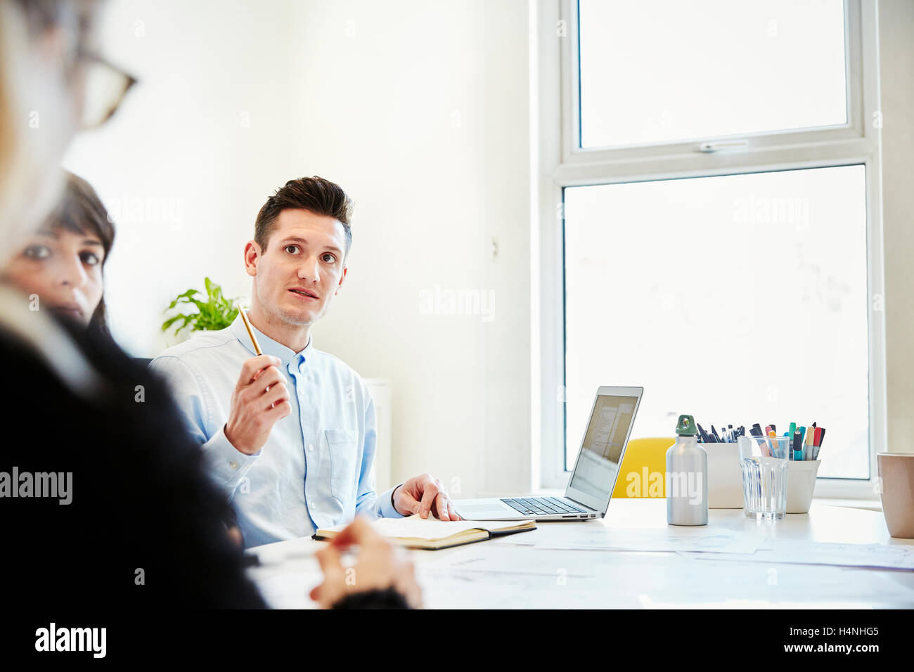A man using a laptop seated at a table talking to two colleagues in ...