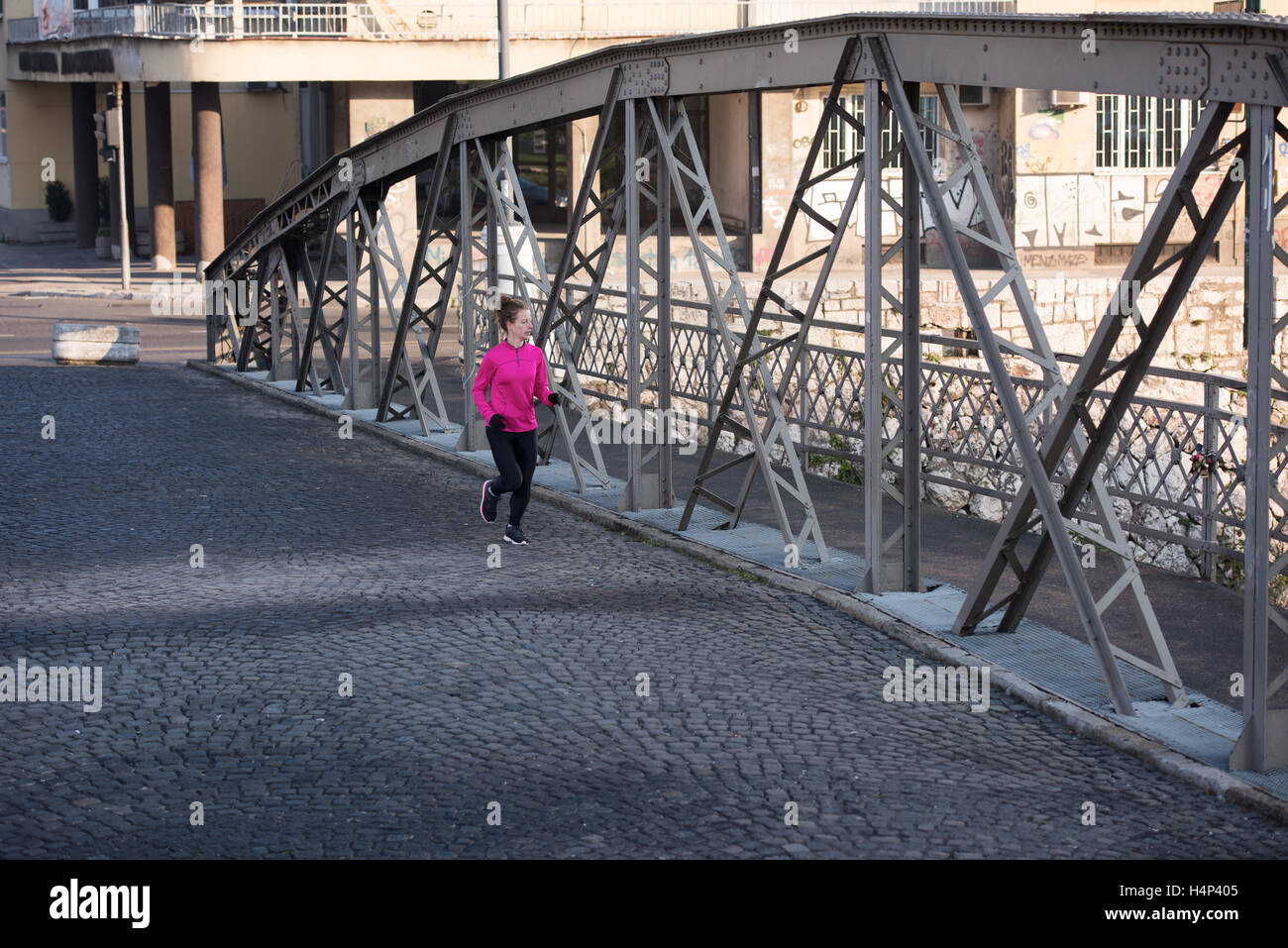 sporty woman running on sidewalk at early morning jogging with city ...