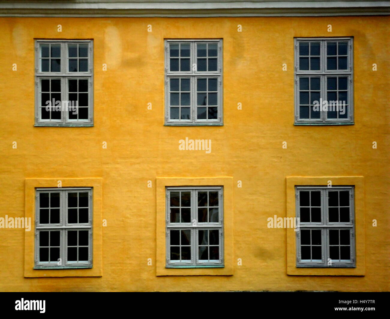 The front of a yellow house with symmetrical and regular grey windows ...