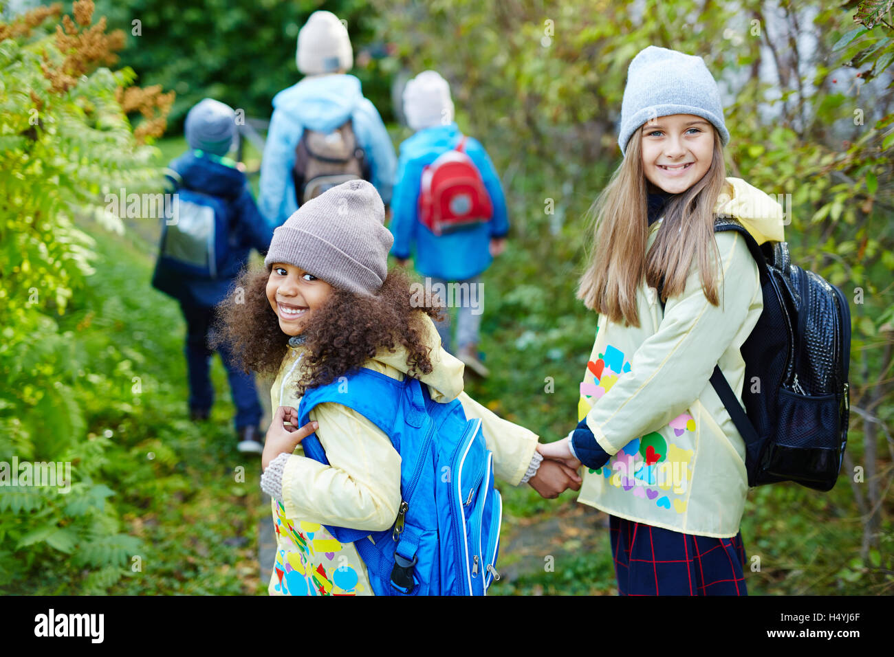 Two happy girls with backpacks looking at camera while walking to ...