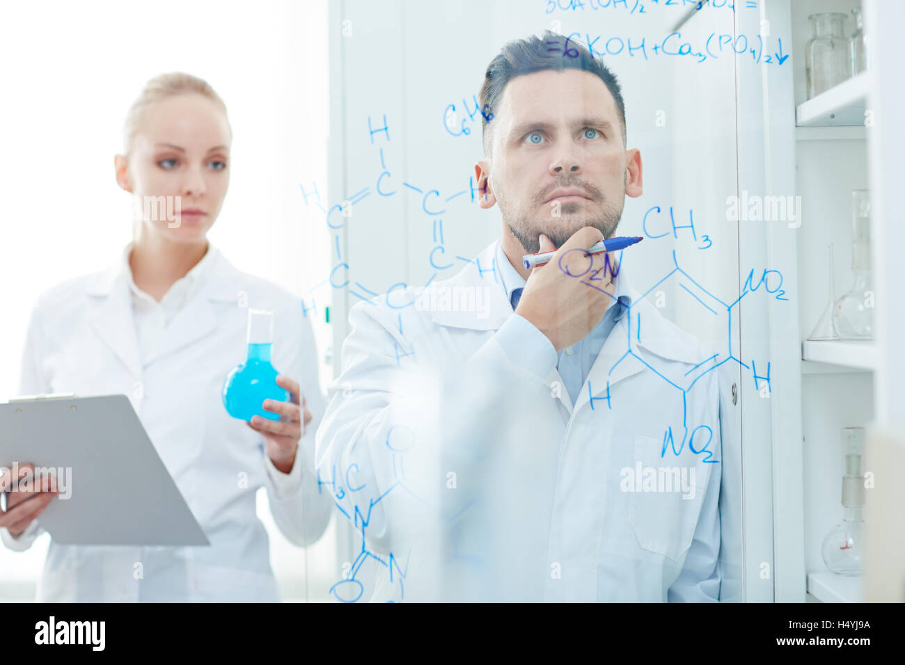 Serious chemist looking at chemical formula on transparent board with ...