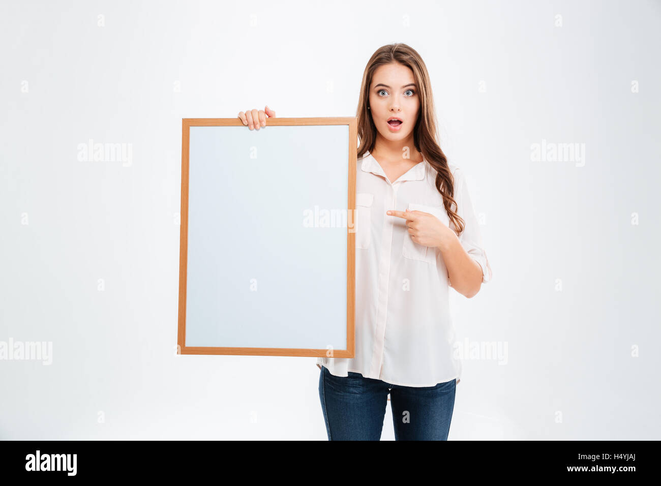Portrait of a smiling woman pointing finger on blank board isolated on ...