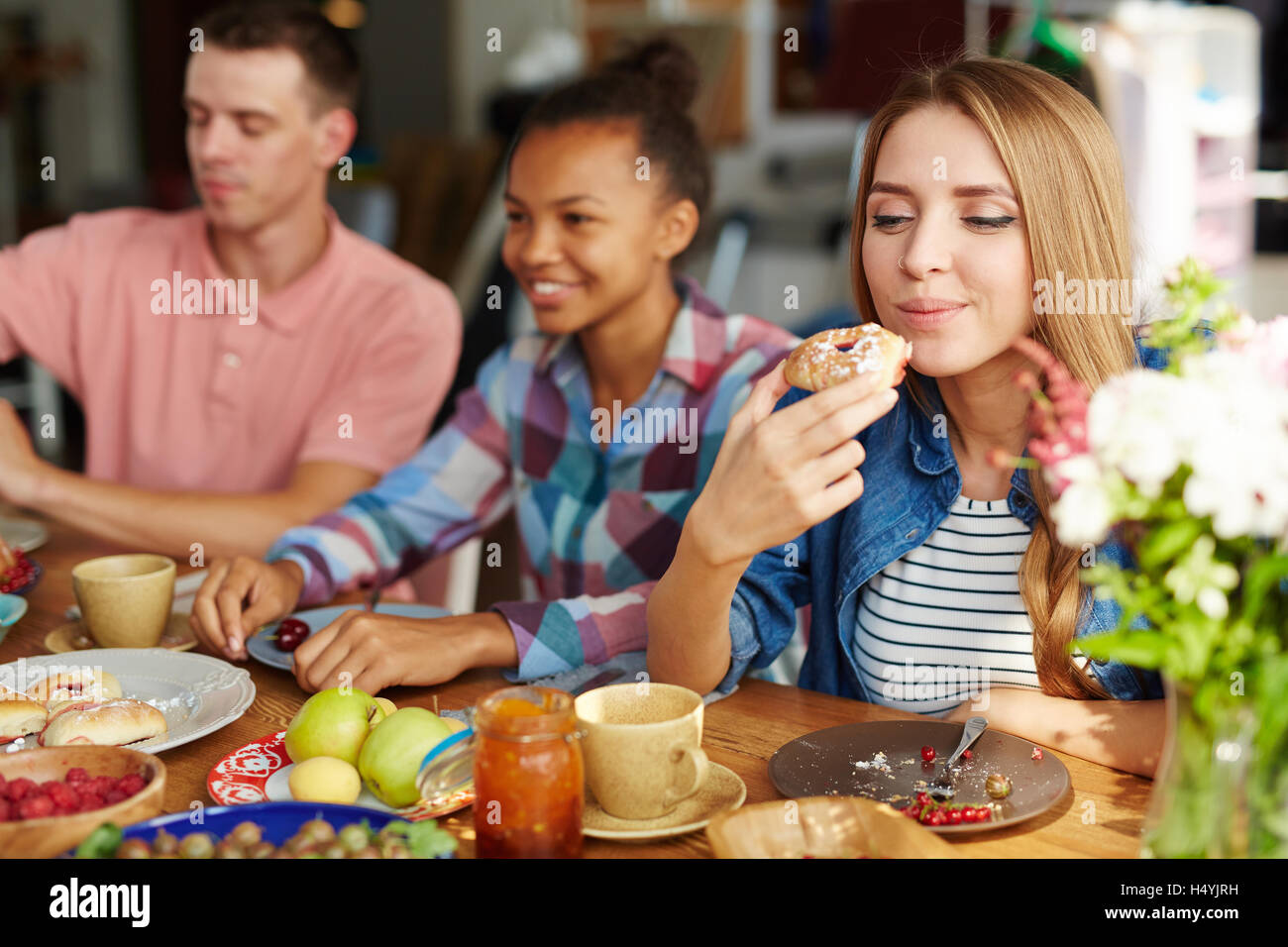 Girl eating pastry among her friends by table Stock Photo - Alamy