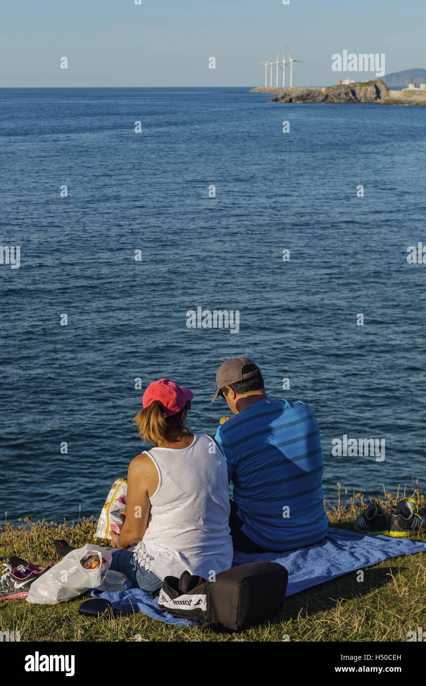 Adult couple eating chips sitting on the edge of a cliff overlooking ...