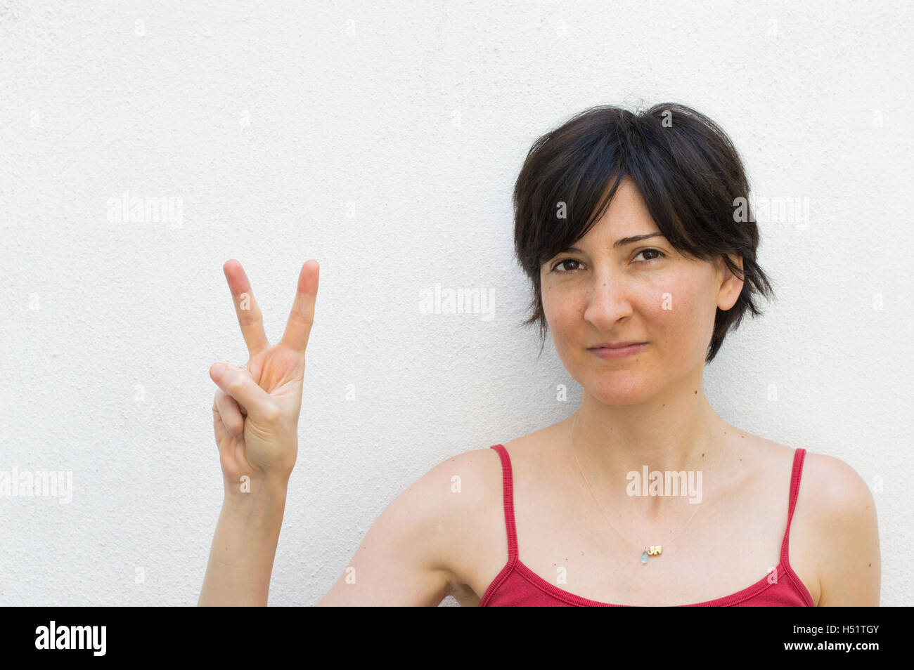 Young Woman Making Peace Sign in Front of a Wall Stock Photo - Alamy