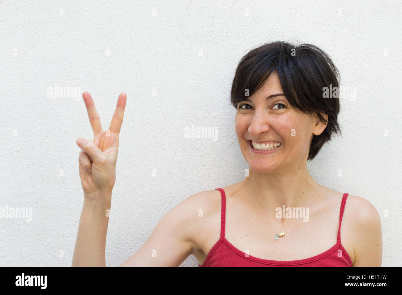 Young Woman Making Peace Sign in Front of a Wall Stock Photo - Alamy