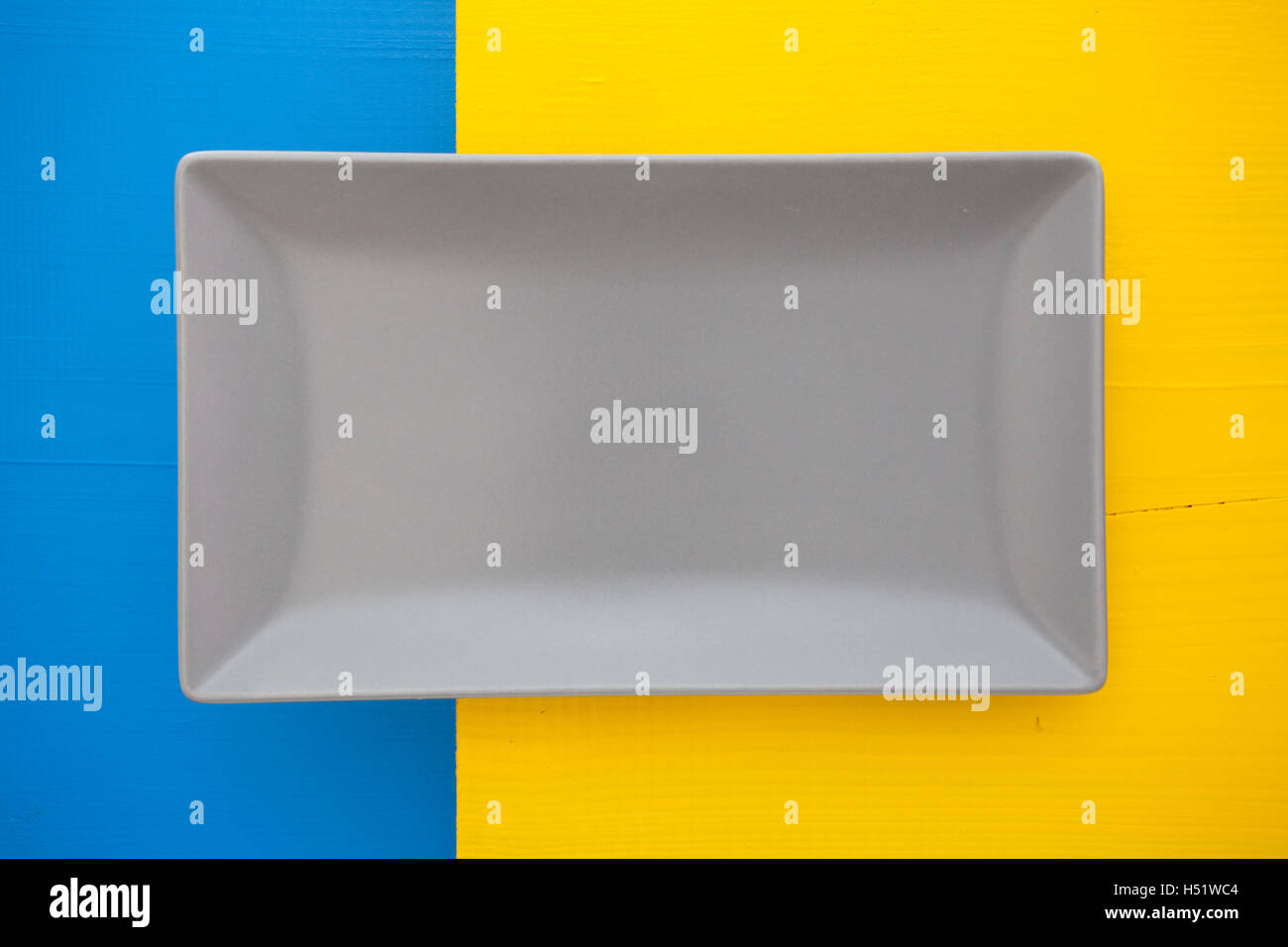 Empty gray ceramic dish on over blue and yellow wooden table, rectangle ...