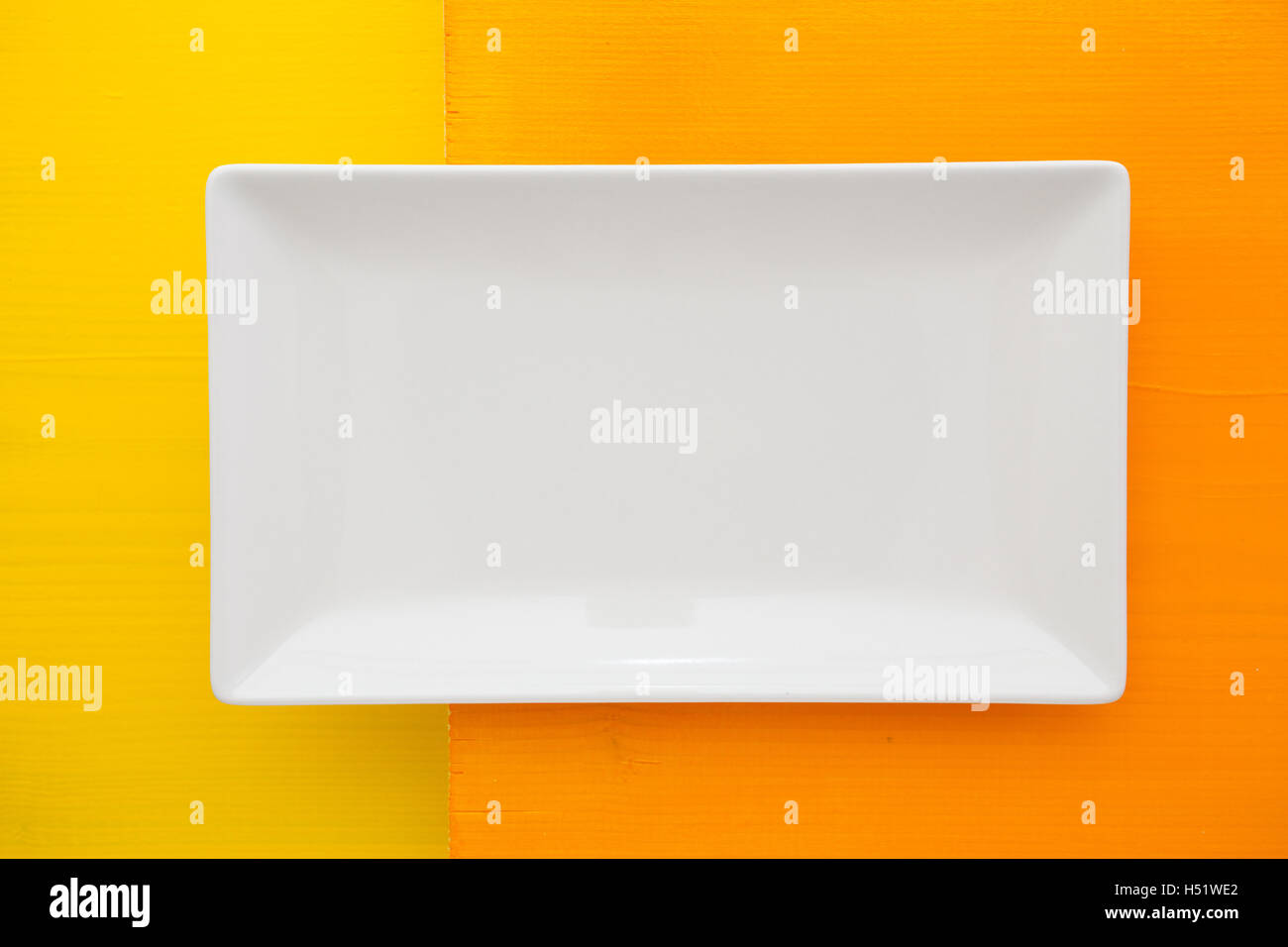 Empty white ceramic dish on over orange and yellow wooden table ...