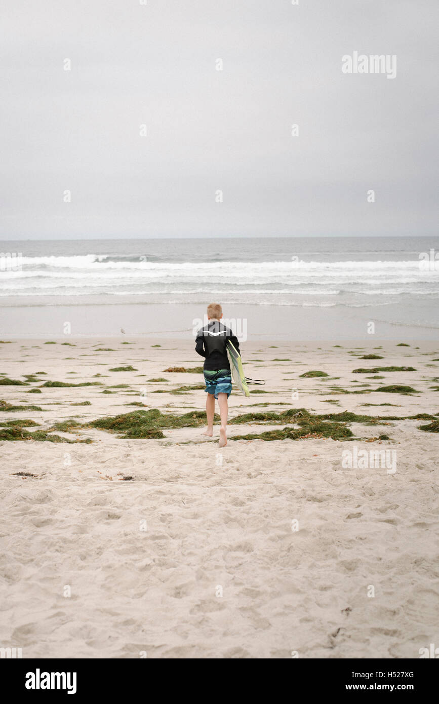 Rear view of a boy carrying a bodyboard, walking into the ocean Stock ...