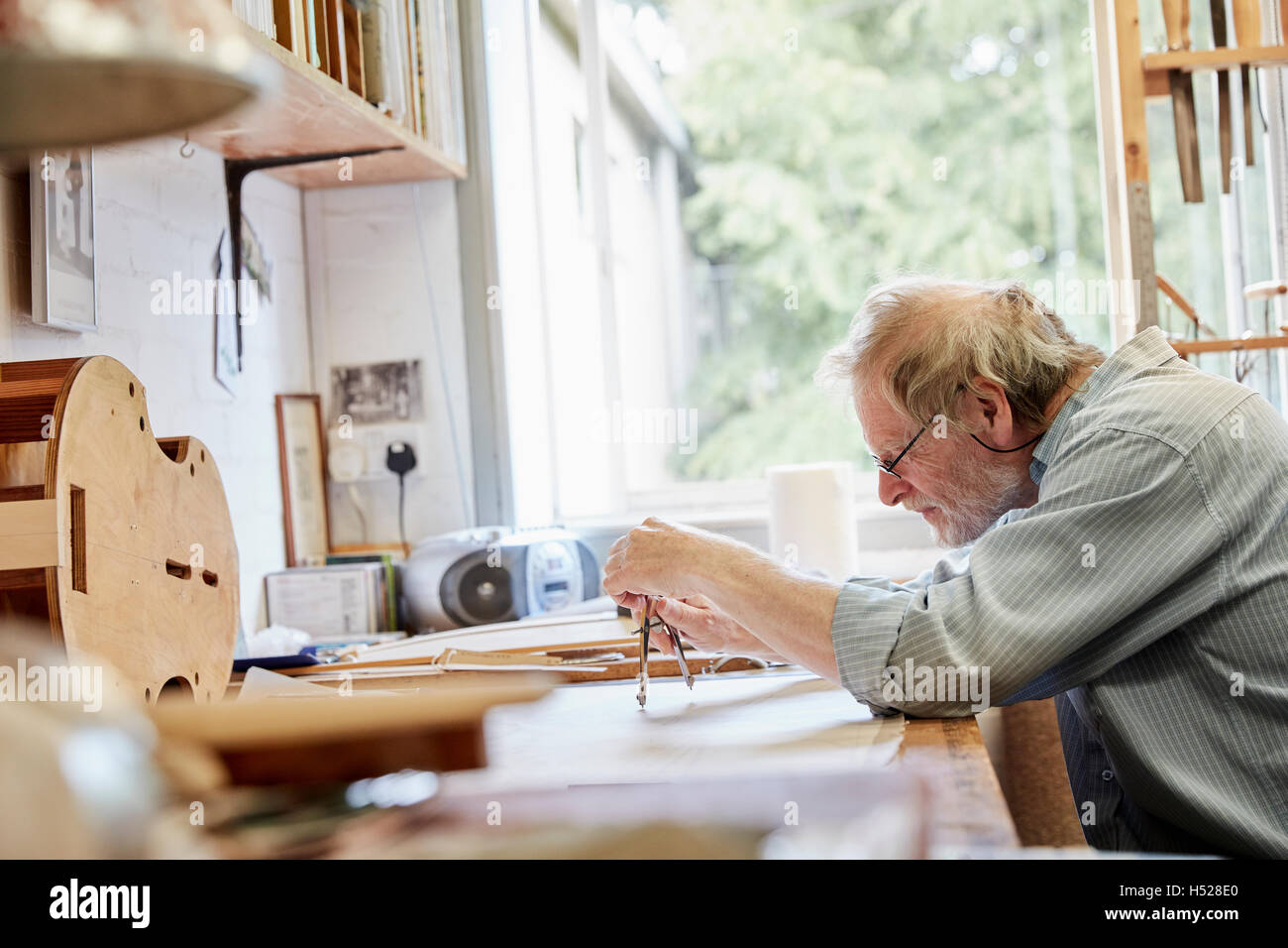 A violin maker at his drawing board drawing out the plans and outline ...
