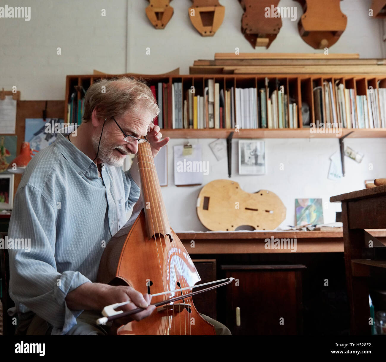 A violin maker in his workshop playing instrument with a bow, tuning ...