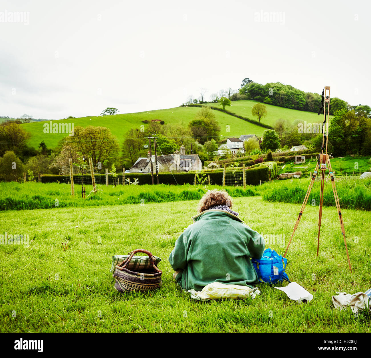 A woman artist working outdoors in the landscape, sitting on the ground ...