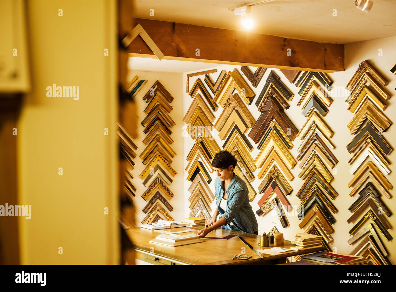 Woman working at a picture framers, a large selection of frames on the ...