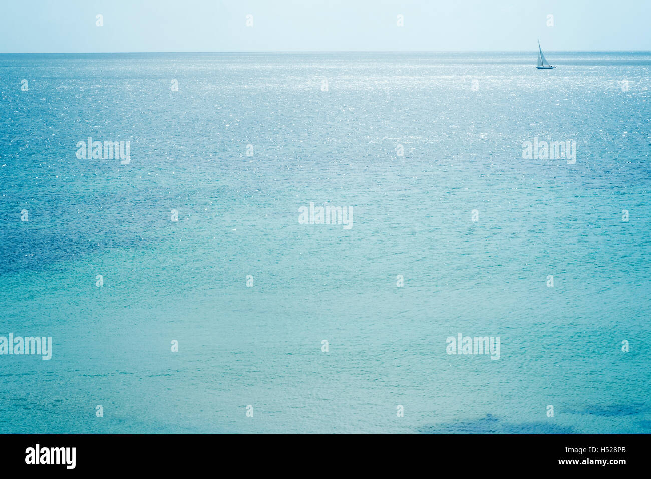 Distant sailing boat on a shimmering blue sea Stock Photo - Alamy