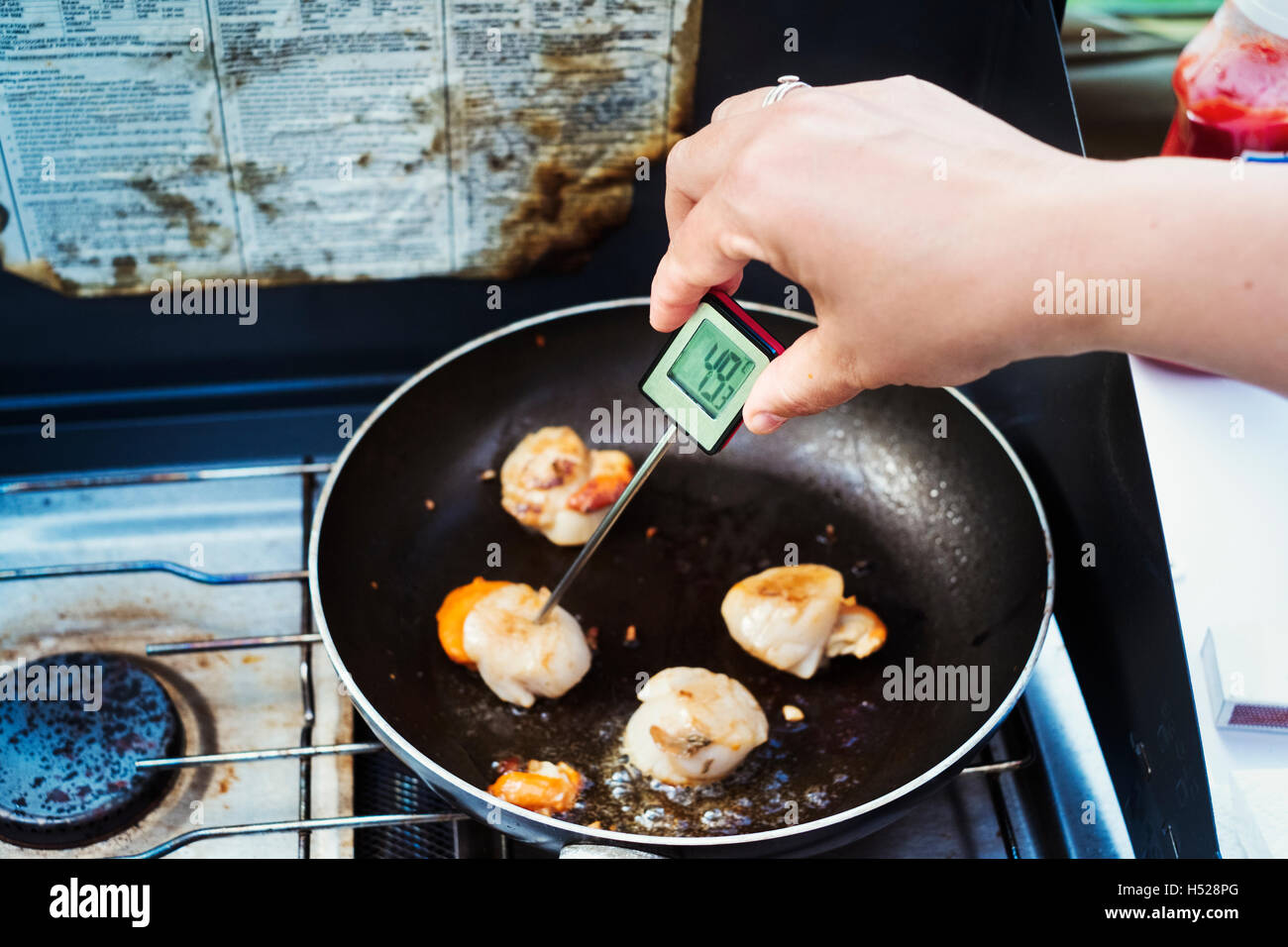 Woman measuring the temperature of a scallop in a frying pan with a ...