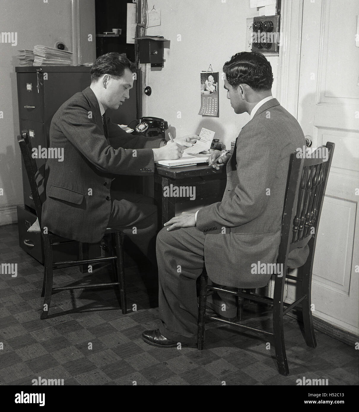 1950s, historical, man sitting in office giving his personal details ...