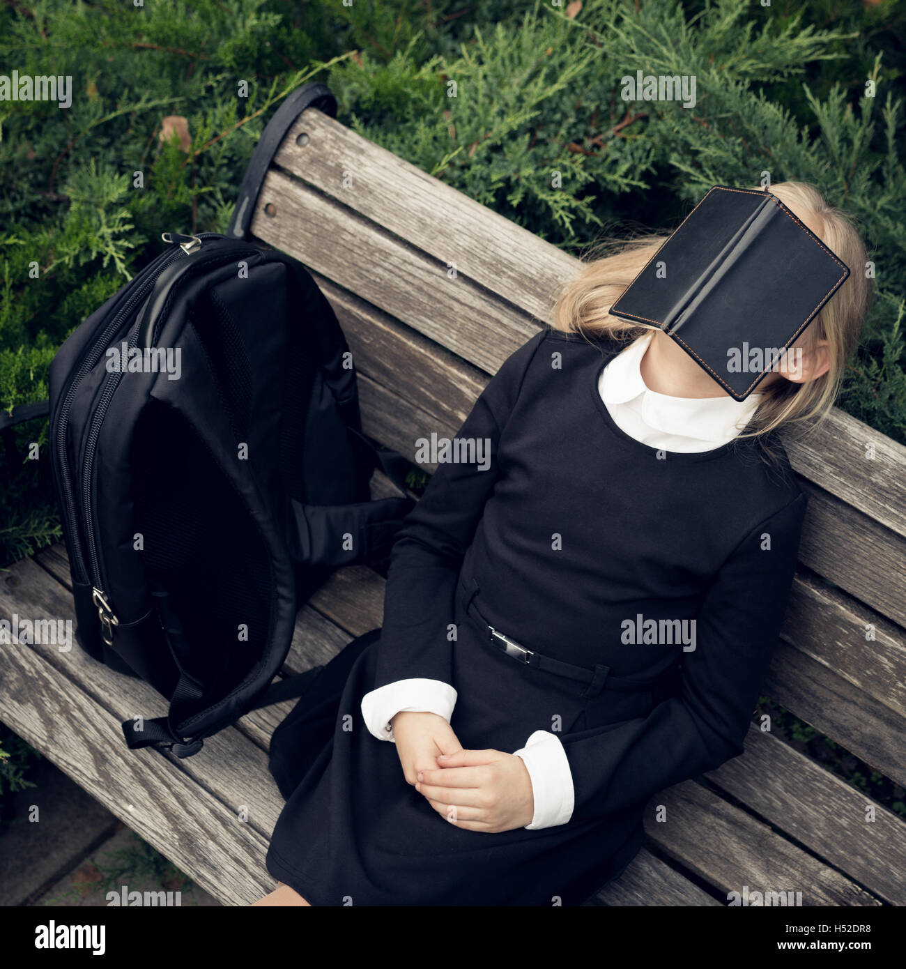 Beautiful blond girl in a school uniform sits on park bench and hiding ...