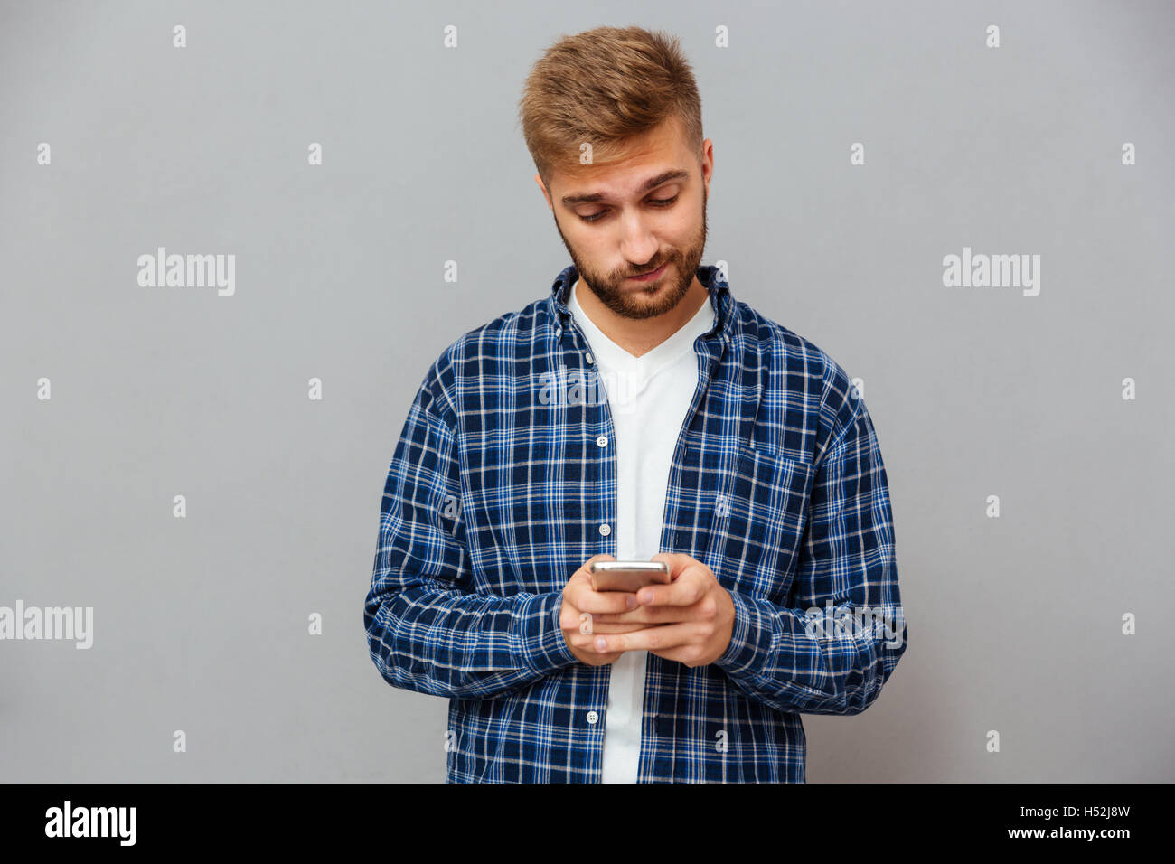 Upset bearded man texting message on smartphone isolated on a gray ...