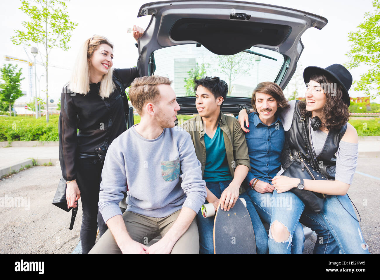 Group of young multiethnic friends sitting in a trunk of a car, talking ...
