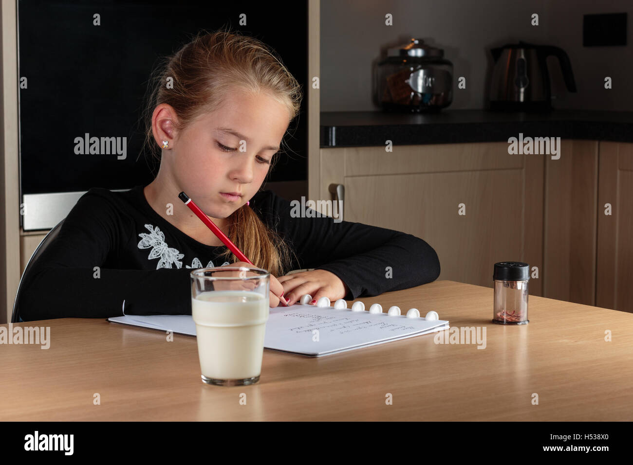 Girl doing homework at the kitchen table with glass of milk Stock Photo ...