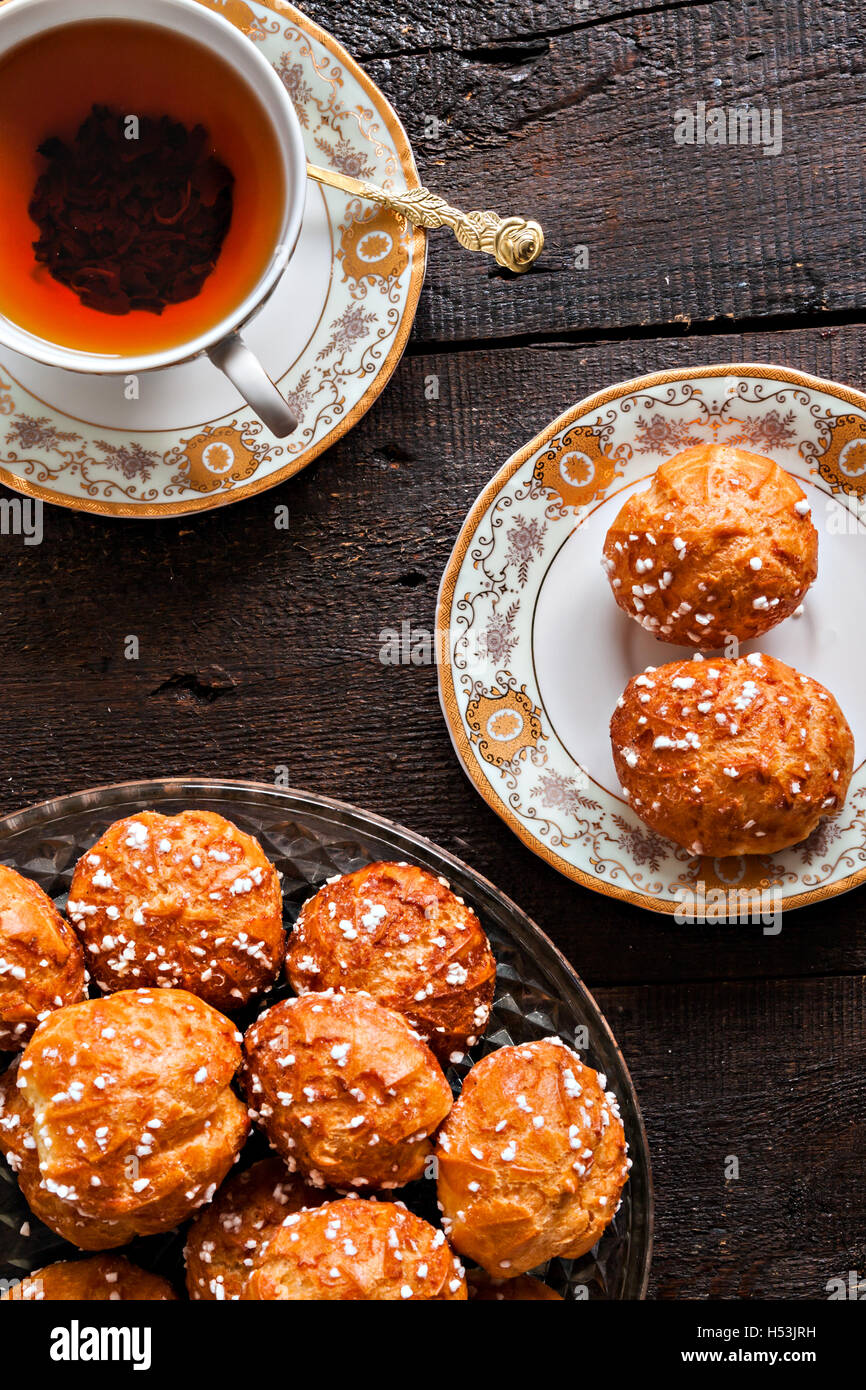 profiteroles topped with sugar and vintage cup with tea on a dark ...
