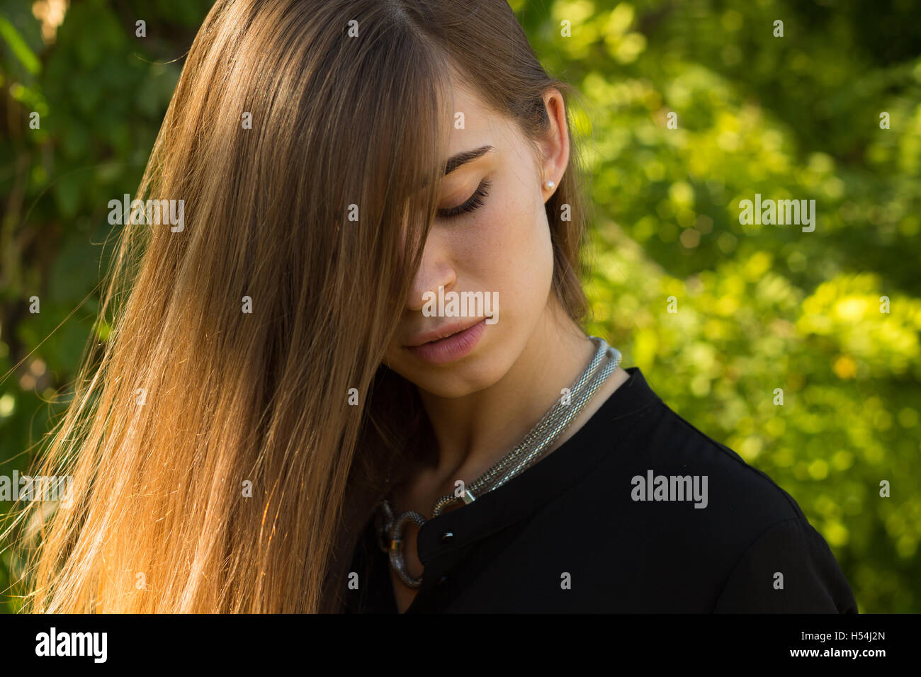 Young woman looking down on the background of trees Stock Photo - Alamy