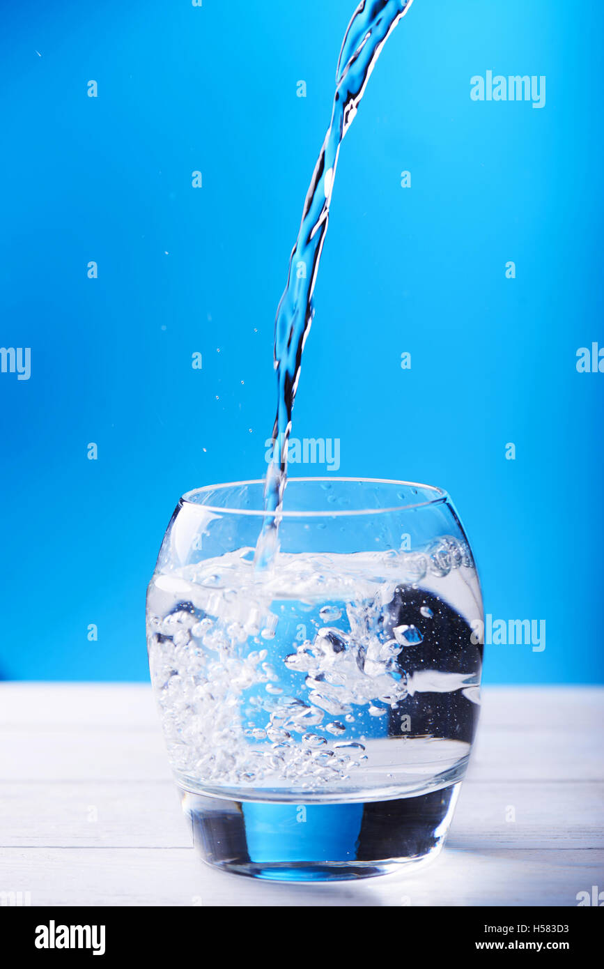 Pouring water with splashes in glass at a blue background Stock Photo ...
