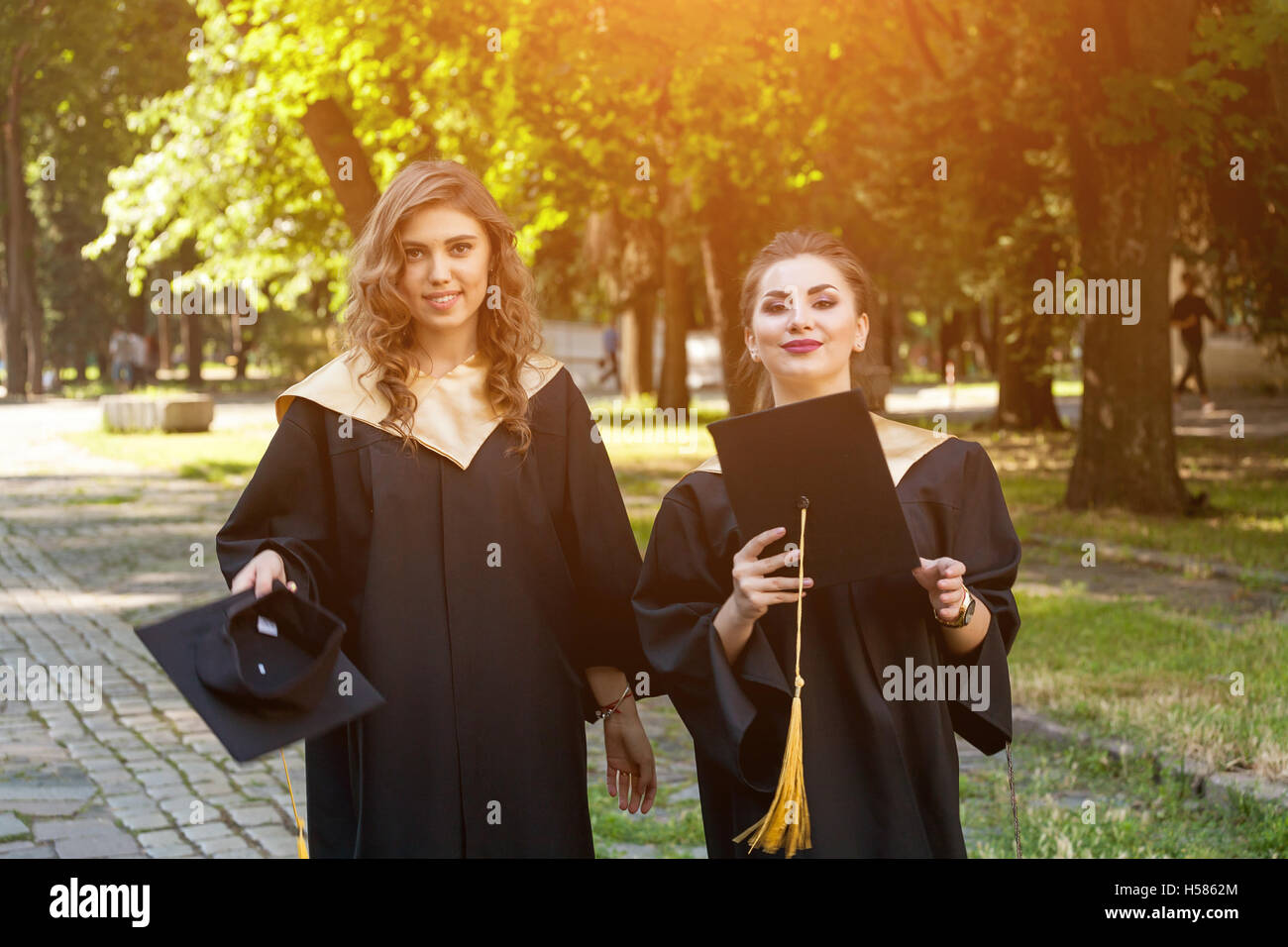 Portrait of two happy students in graduation gowns on university campus ...