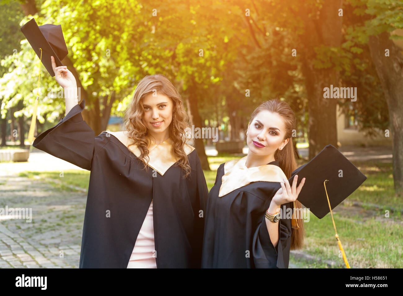 Portrait of two happy students in graduation gowns on university campus ...