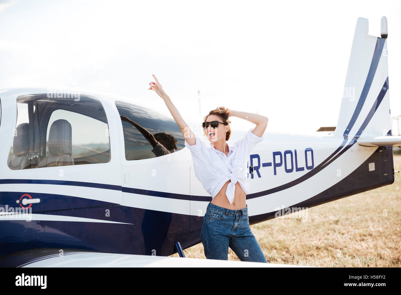 Attractive young woman posing near a plane and pointing finger up ...