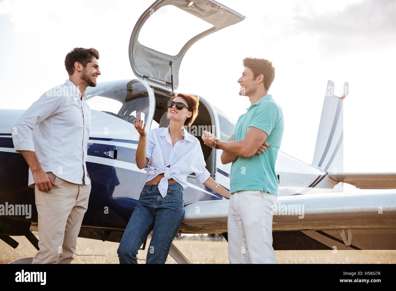 Three happy young friends standing and talking near small plane Stock ...