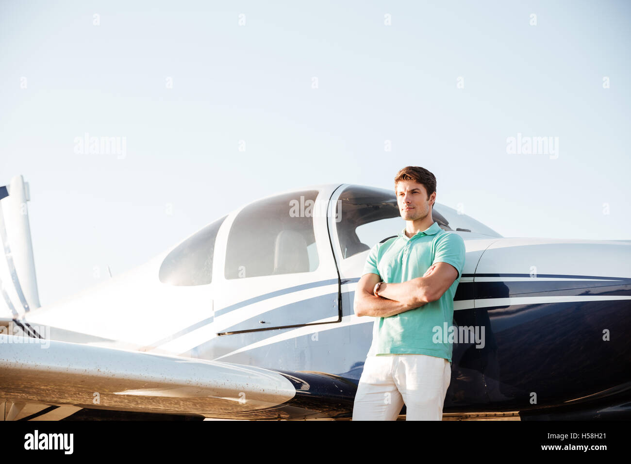 Confident young man standing with arms crossed in front of small ...
