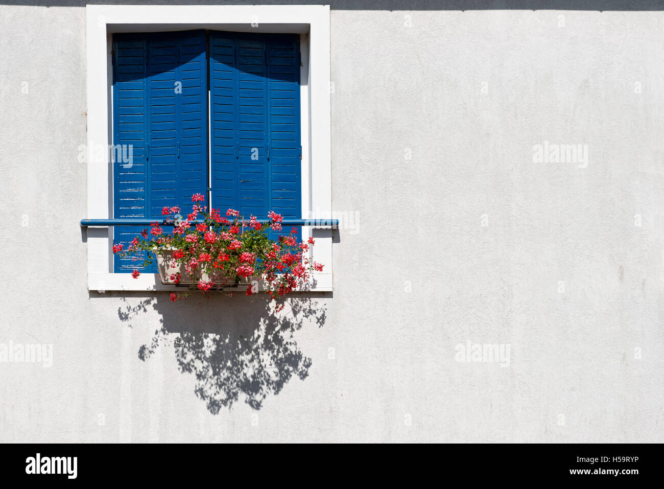 A typical blue shuttered window with flowers in a window box in a ...