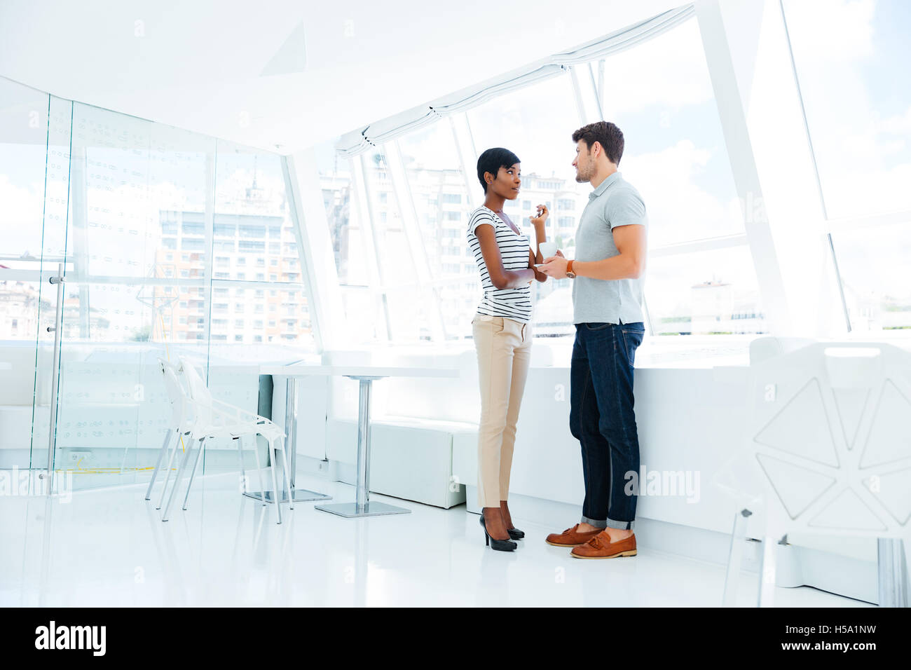 Two young business people standing and talking in office during coffee ...