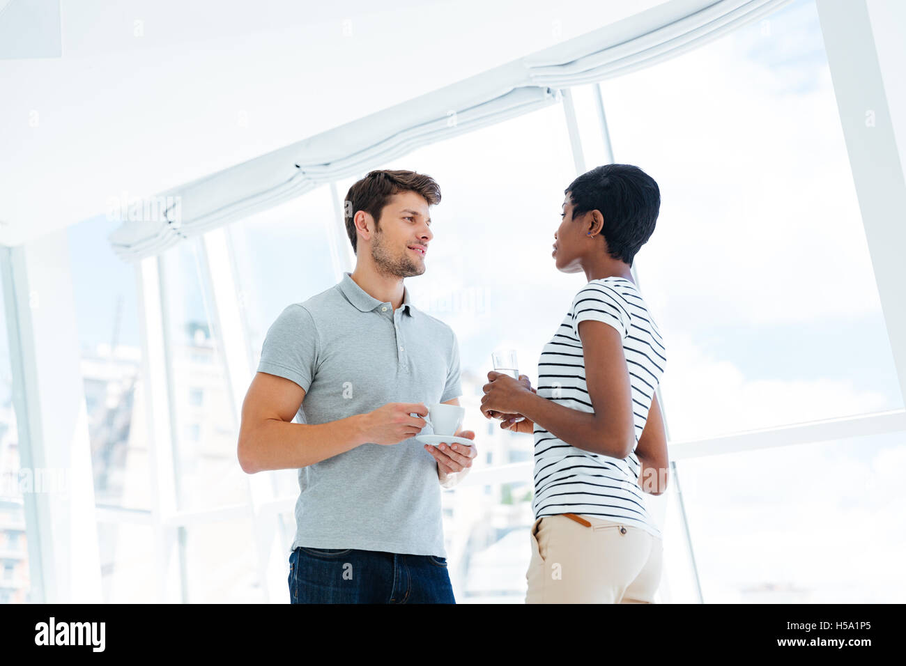 Two young business people standing and talking in office during coffee ...
