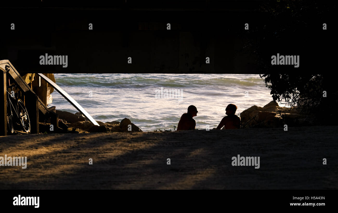 Two men converse under a bridge on the beach Stock Photo - Alamy