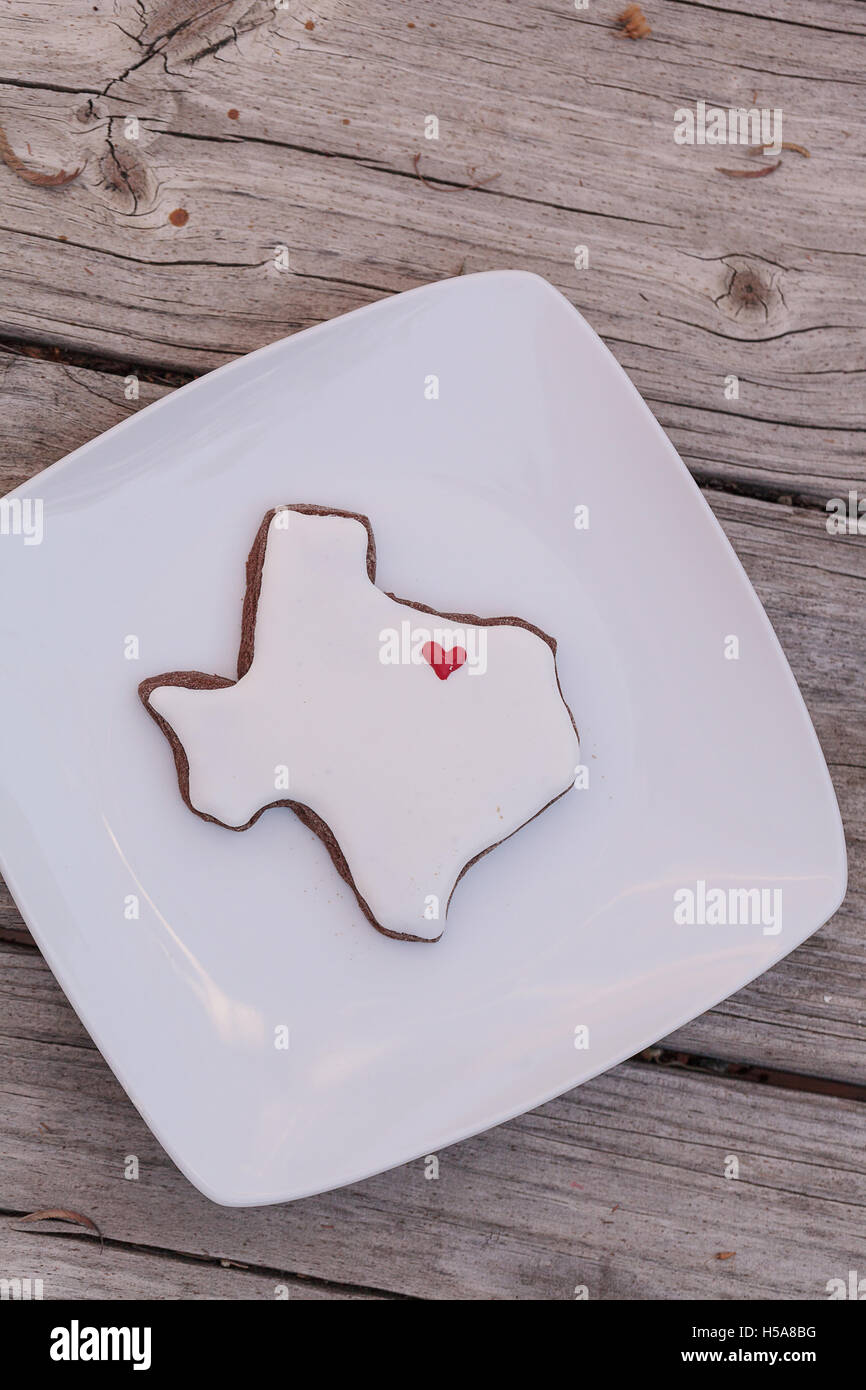 Texas shaped sugar cookie with white icing and a red heart on a rustic ...