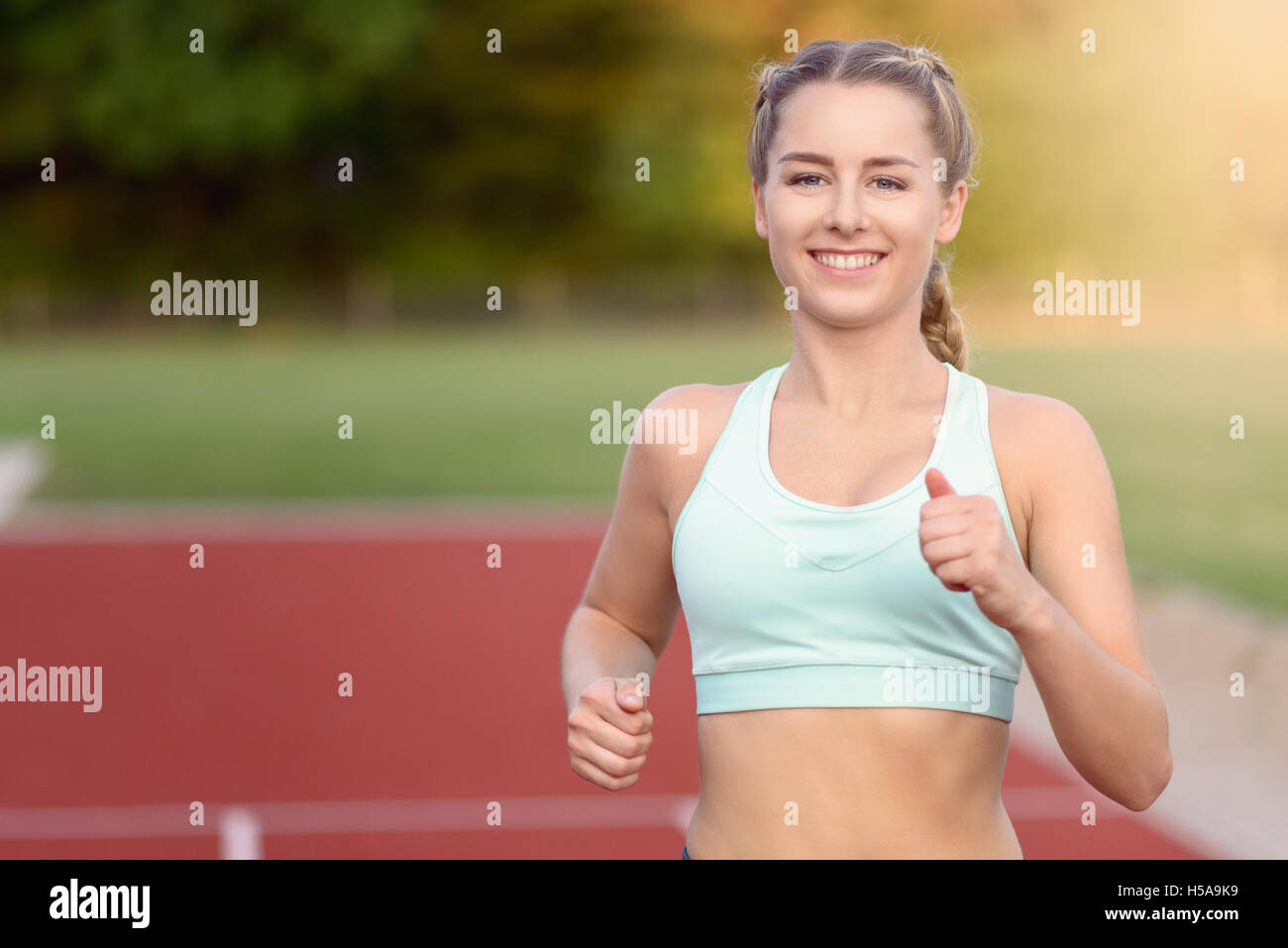 Cute young female runner in tank top with race track and trees in ...