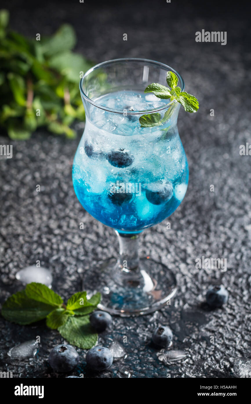 Blueberry cocktail with ice and mint in a glass, over black background ...