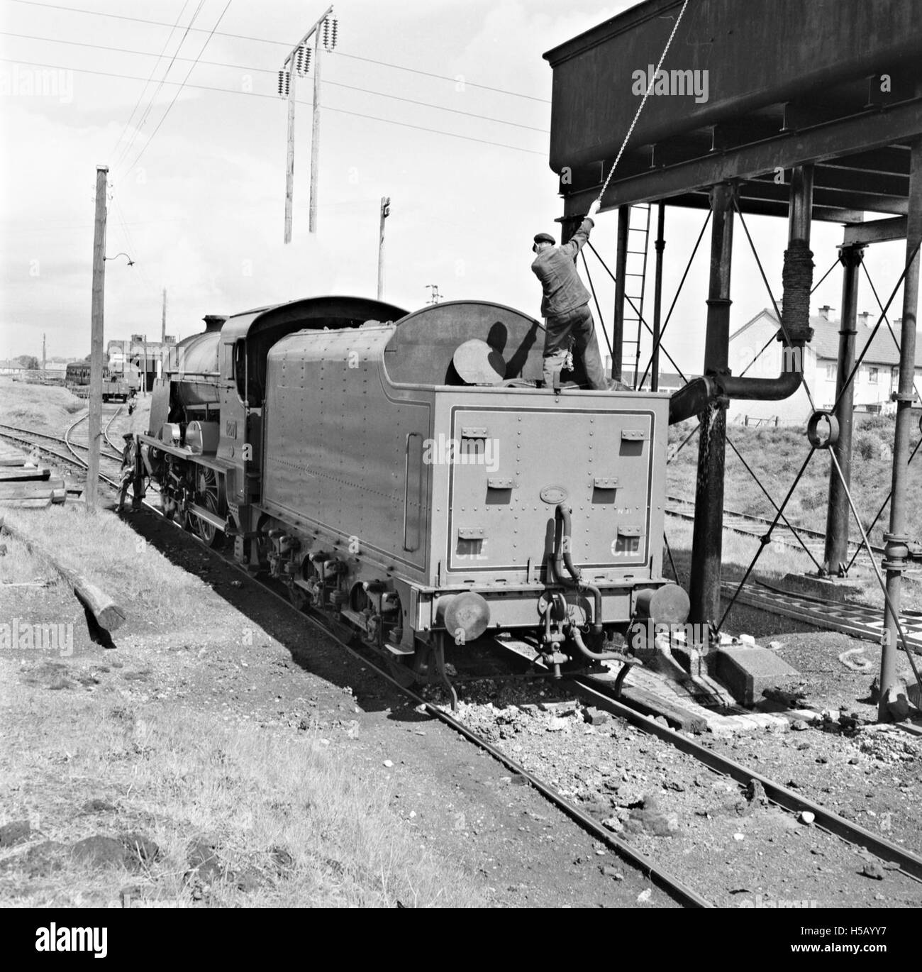 A photograph showing a woman filling up a vehicle at a gas station. The ...