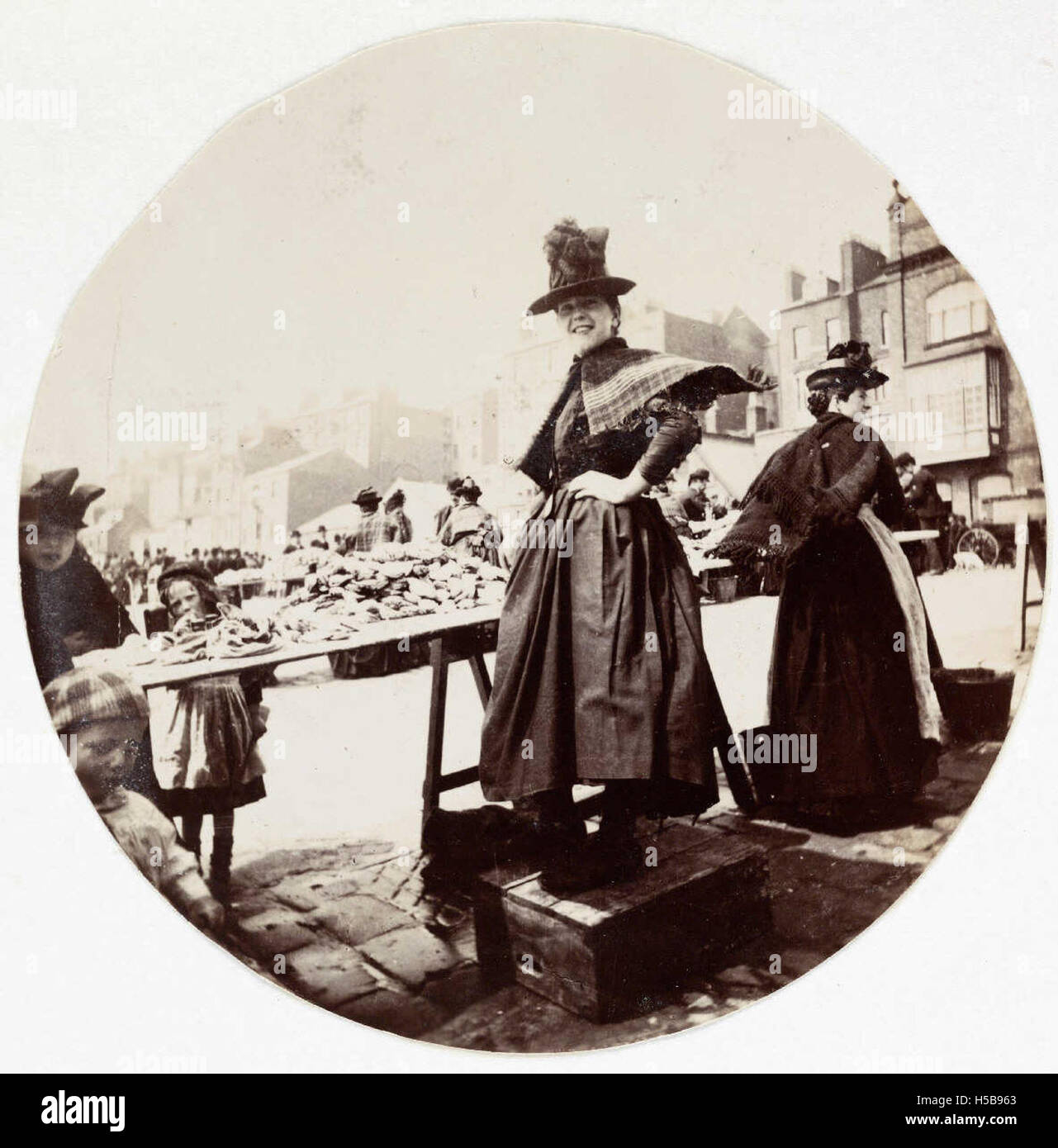 This photograph depicts a woman standing at a market stall. She may be ...