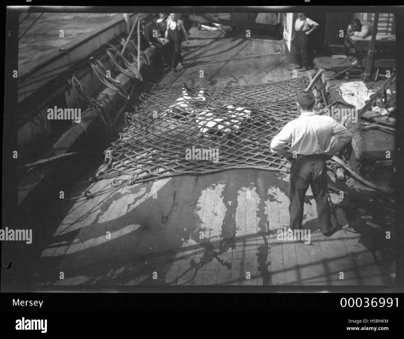 The image shows eight cadets maneuvering under nets aboard the vessel ...