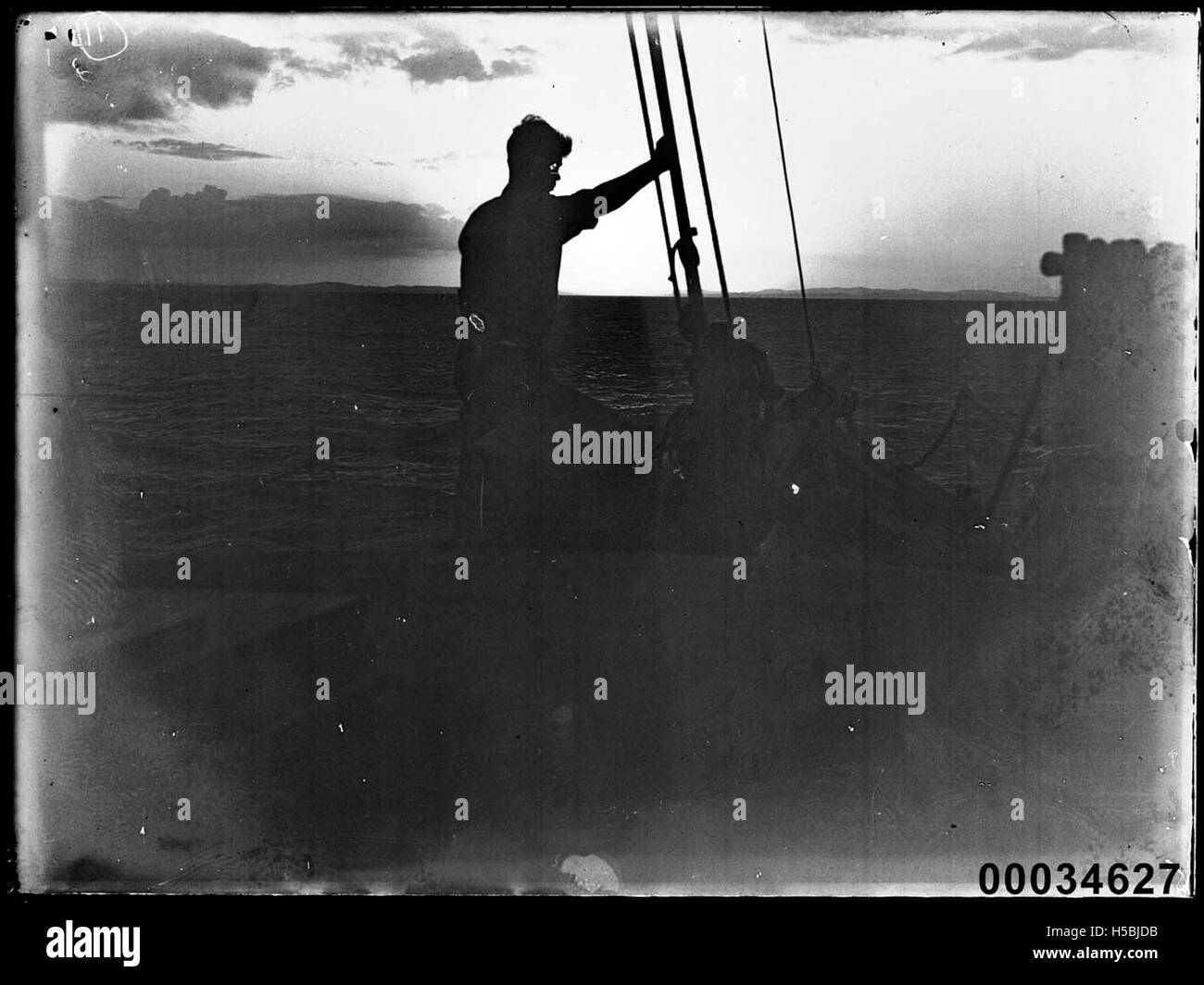 This image shows a man working with rigging near the bow of a ship ...