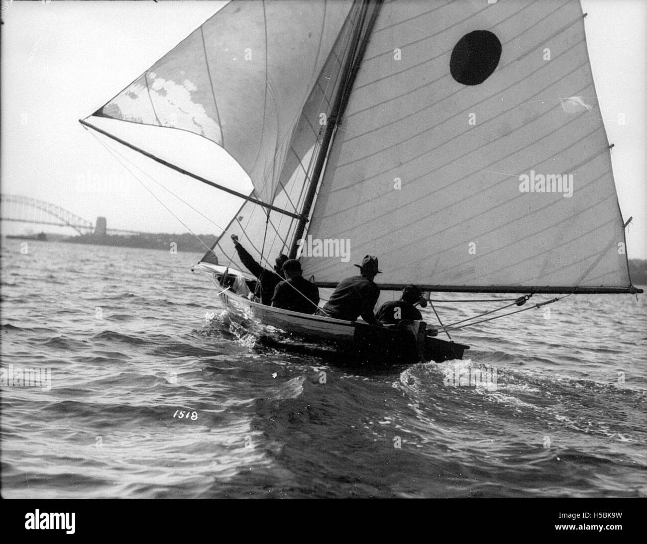 This photograph shows a sloop sailing on Sydney Harbour, with the ...
