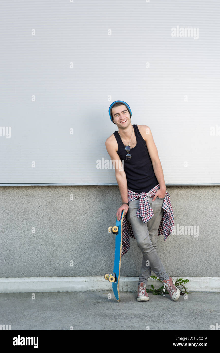 Hip cool urban fashion skateboarder on the street in front of iron wall ...