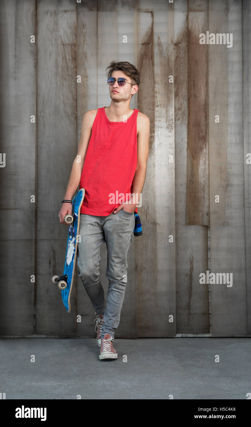 Hip cool urban fashion skateboarder on the street in front of iron wall ...