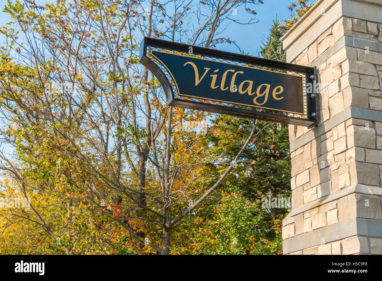 Ornate Village sign on stone pillar with autumn trees in background ...