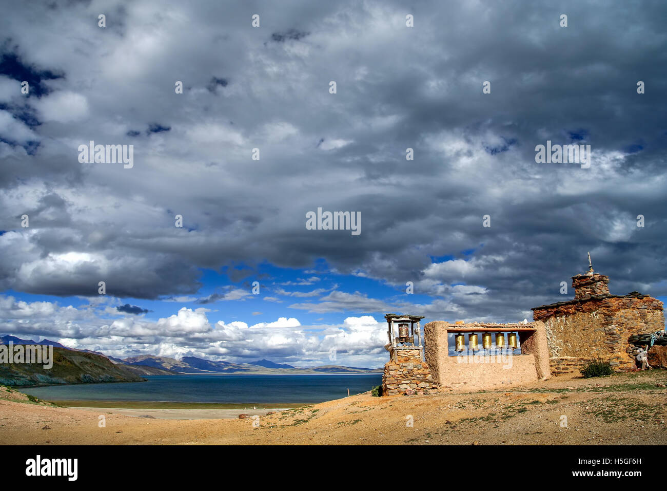 Small old Tibetan monastery and praying mills on a hill above holy Lake ...