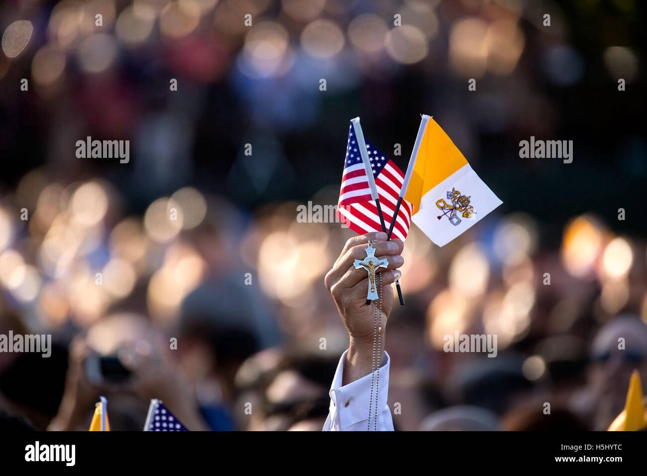 A guest holds up the American flag, the Vatican City flag, and a cross ...