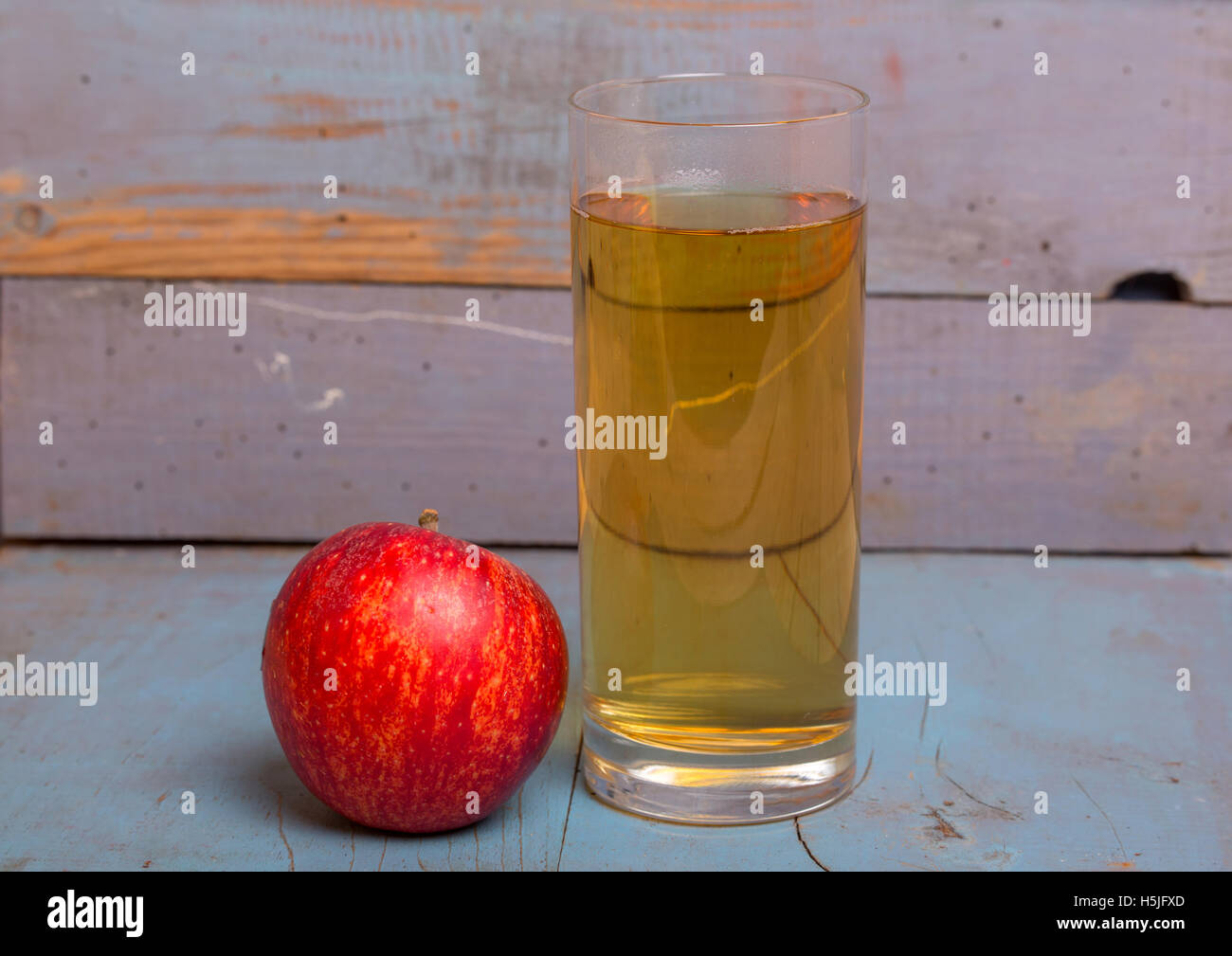 Glass of apple juice and a red apple on a blue old wooden background ...